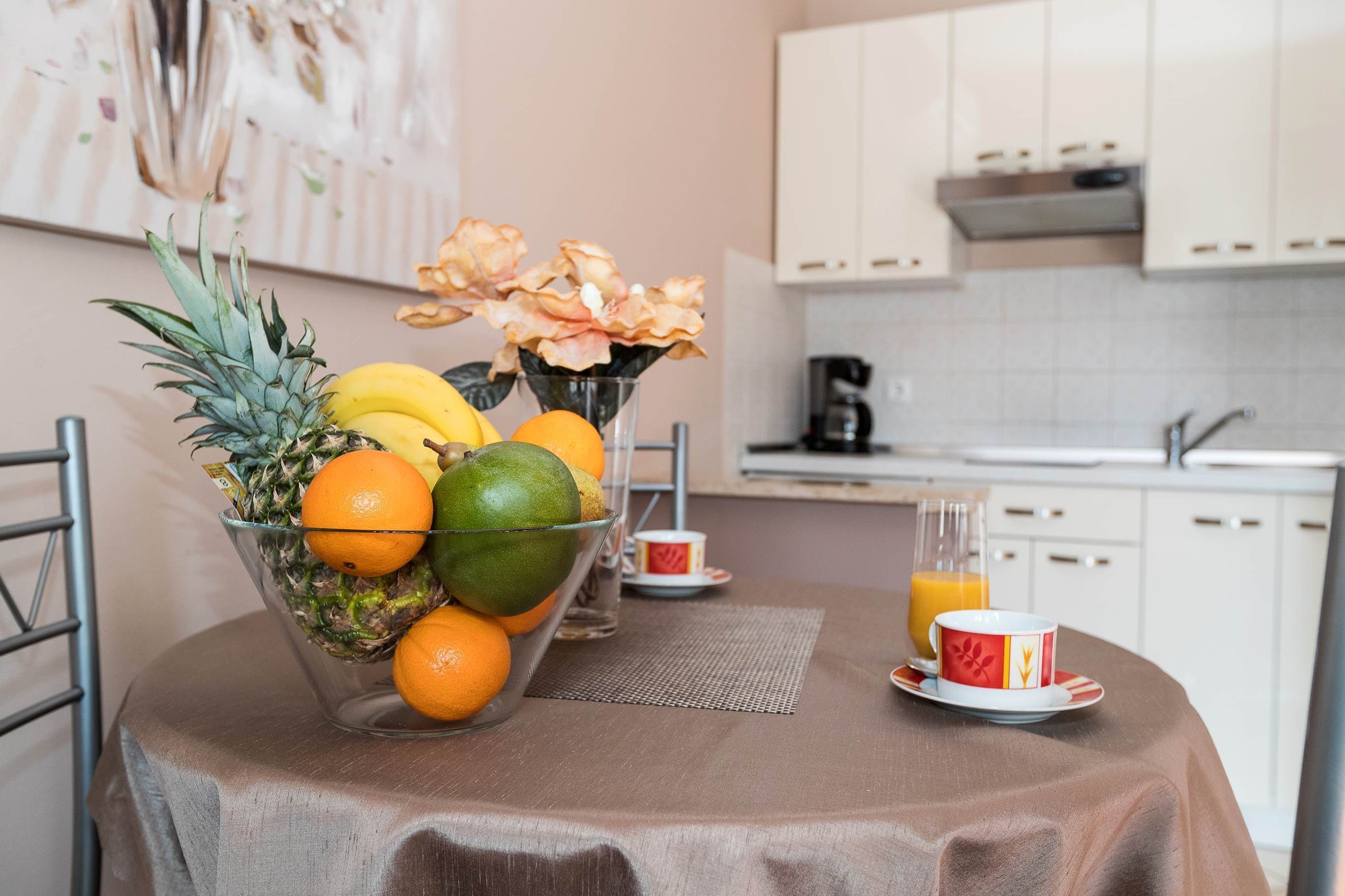 Uma mesa de café da manhã com uma fruteira, um vaso com flores e um copo de suco de laranja.
