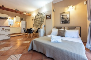 Quarto com cama, escrivaninha e pequeno espaço de cozinha.