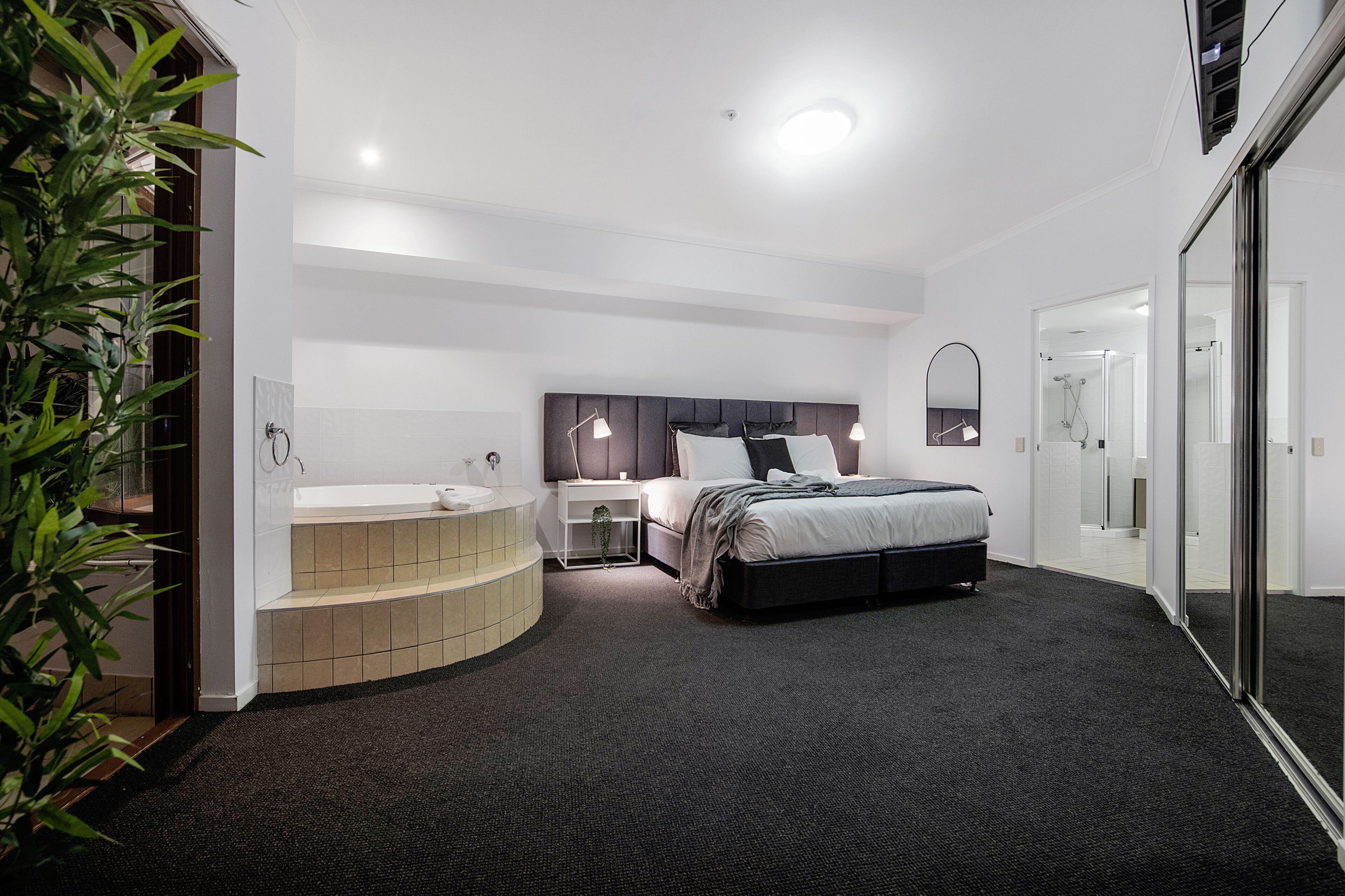 Quarto moderno com uma cama grande, uma banheira em formato de curva e área de chuveiro de vidro.