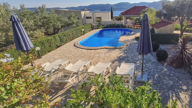 Piscina com espreguiçadeiras, rodeada por azulejos de pedra e vegetação, com montanhas ao fundo.