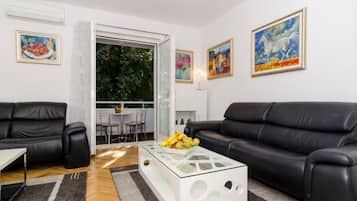 Uma sala de estar com dois sofás de couro preto, uma mesa de centro de vidro com frutas, e obras de arte nas paredes.