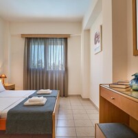Quarto de hotel com uma cama, duas mesas de cabeceira, uma escrivaninha e uma janela com cortinas.