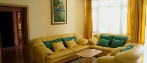Uma sala de estar com um sofá amarelo, uma mesinha de centro e um quadro de araras na parede.
