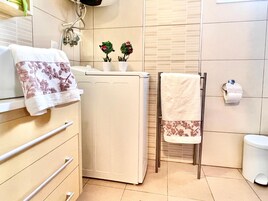 Uma casa de banho compacta com máquina de lavar, porta-toalhas, sanita e uma pequena planta na parede.