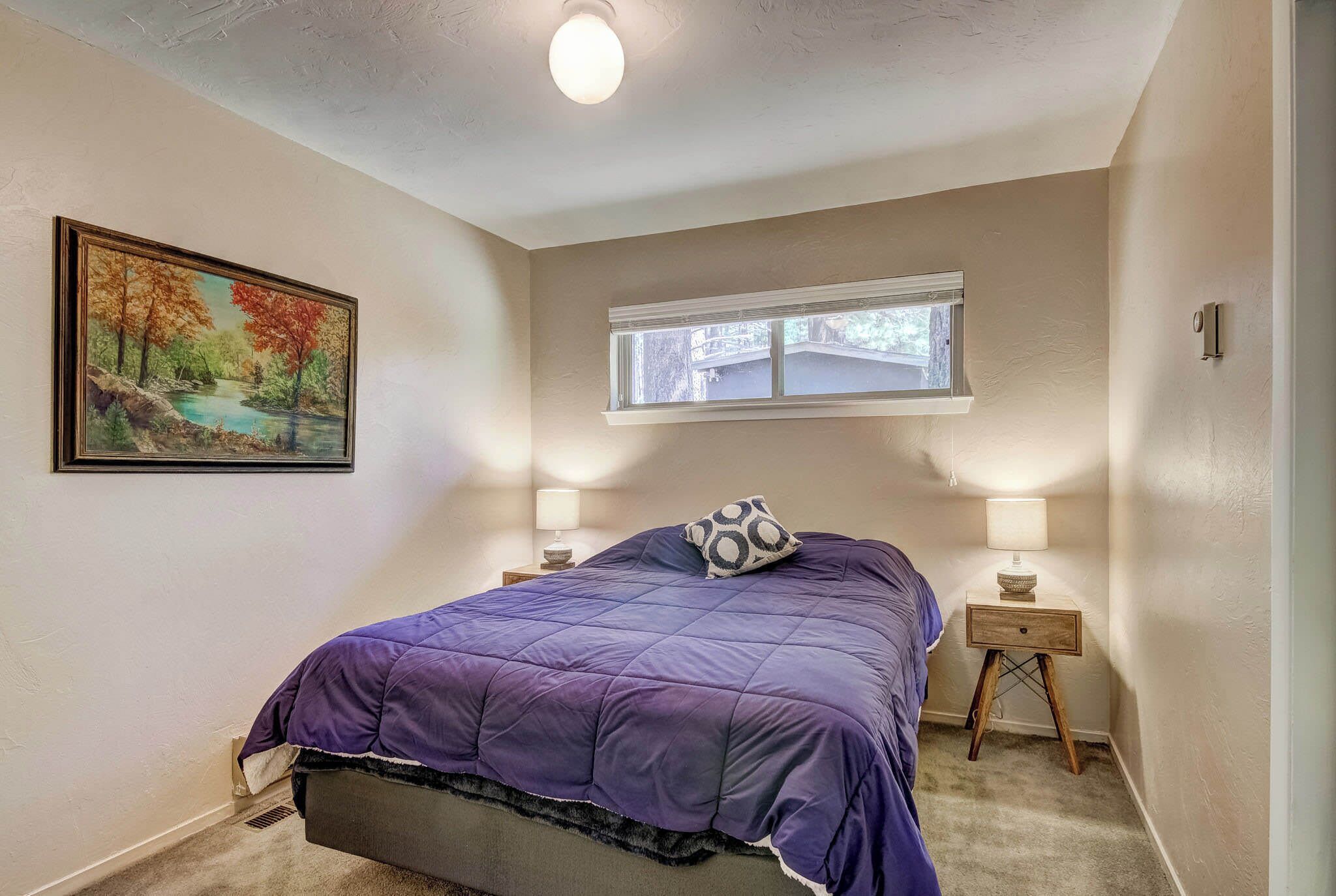 Quarto com cama, janela, mesa de cabeceira, luminária e um quadro na parede.