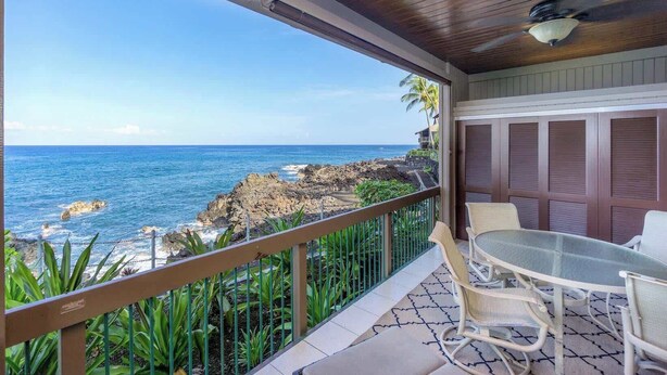 Varanda com mesa e cadeiras de vidro com vista para a costa rochosa e o oceano.