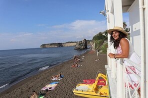 Uma praia com pessoas se banhando ao sol, um penhasco rochoso ao fundo e um edifício com fachada branca.
