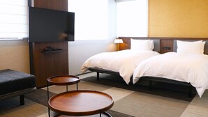Quarto de hotel com cama, duas mesas de cabeceira, televisão e janela com persianas.