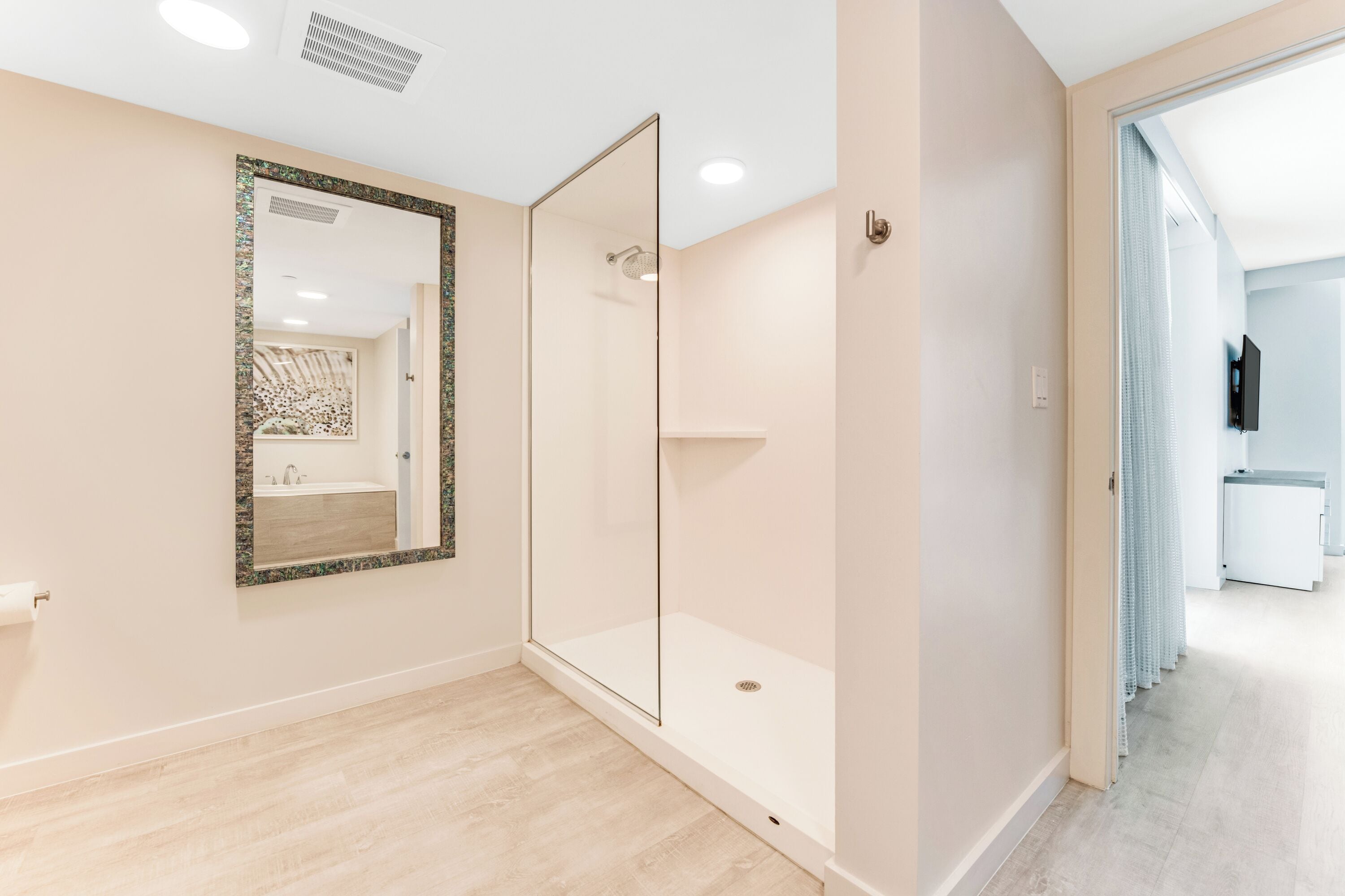 Uma casa de banho moderna com cabine de duche em vidro, um espelho grande com moldura decorativa e um chão de cor clara.