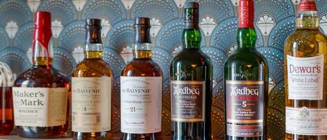 Várias garrafas de whisky dispostas numa prateleira, com um fundo de parede em azulejos estampados.