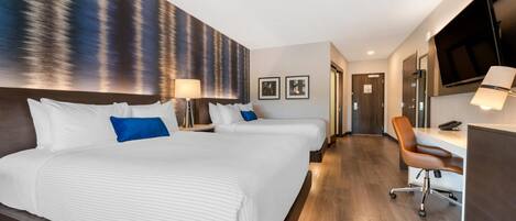 Quarto de hotel com duas camas, uma escrivaninha, uma cadeira e uma televisão.
