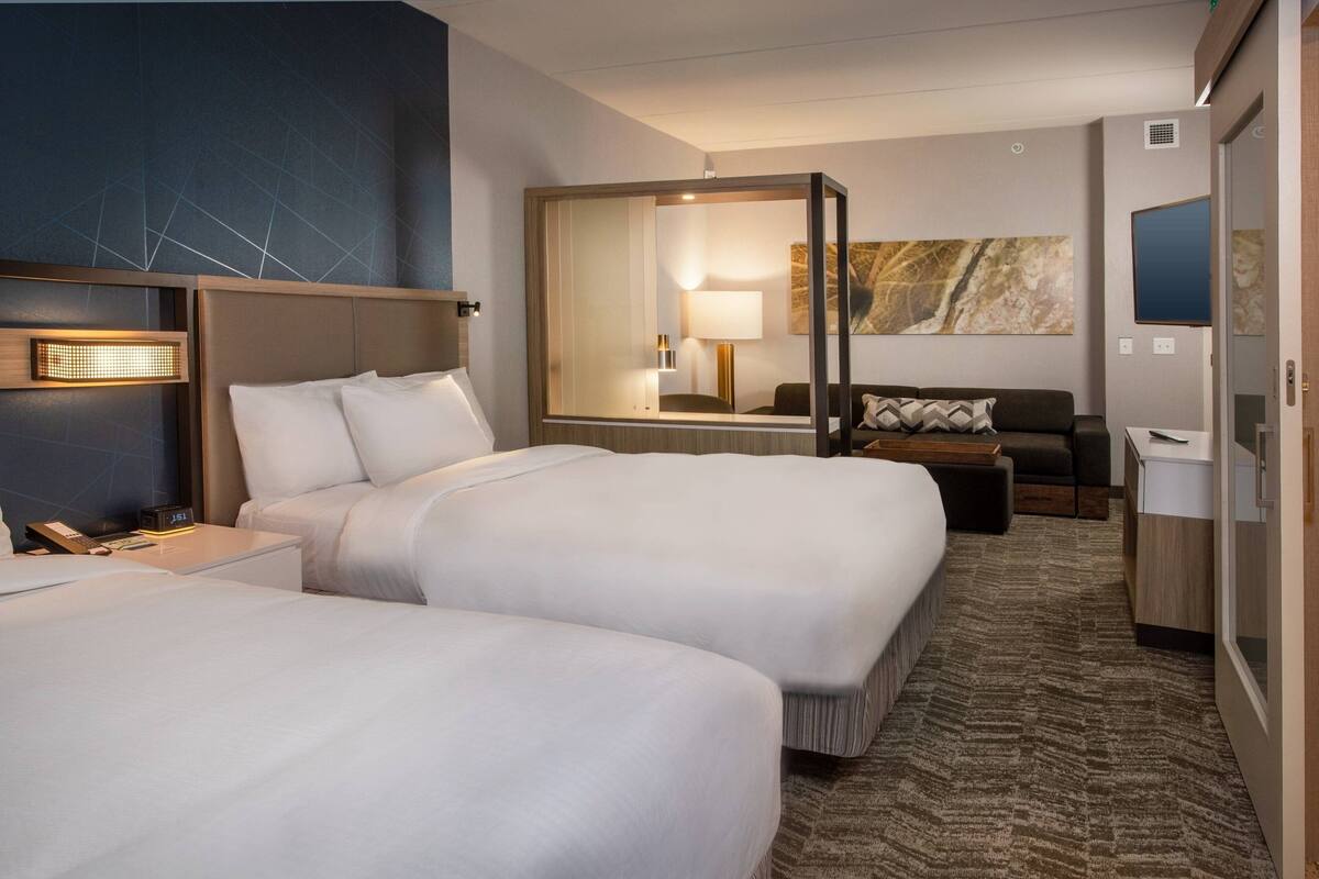 Quarto de hotel com duas camas, um espelho grande, um sofá, uma escrivaninha e um banheiro.