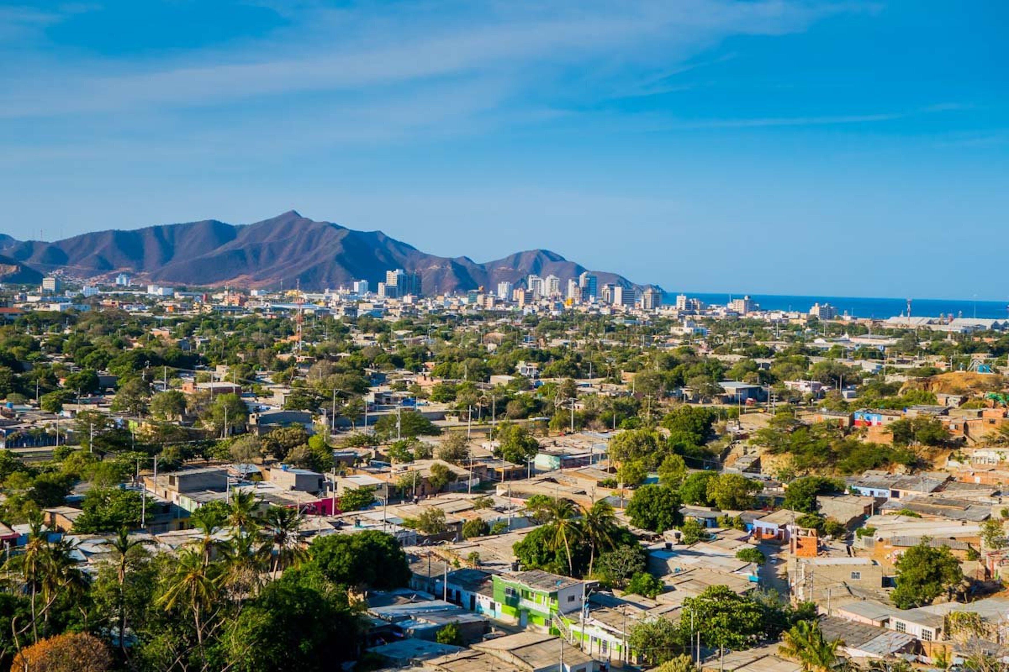 Paisagem urbana com edifícios residenciais e comerciais, uma cordilheira ao fundo e céu azul límpido.