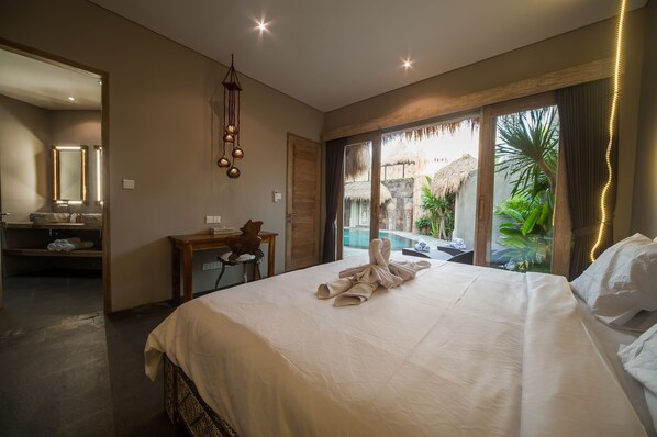 Quarto de hotel com uma cama grande, uma escrivaninha, uma cadeira, um espelho e vista para uma piscina e áreas verdes.