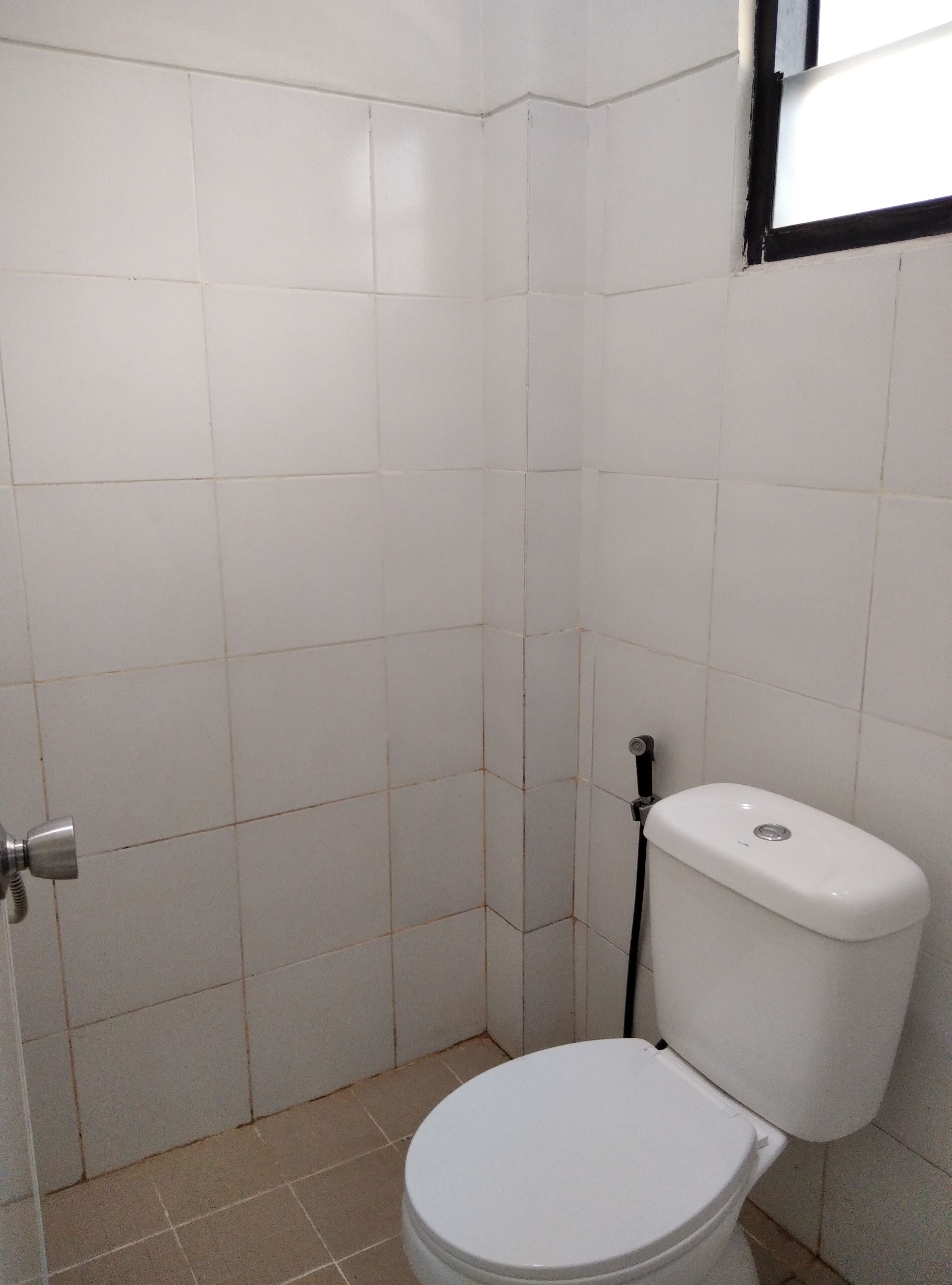 Casa de banho pequena e limpa, com azulejos brancos, sanita branca e área de duche.
