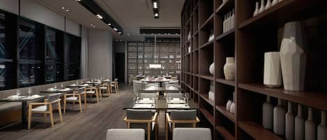 Um restaurante moderno com mesas compridas, cadeiras de madeira e uma variedade de vasos de cerâmica branca em prateleiras.