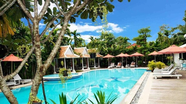 Piscina com espreguiçadeiras e guarda-sóis, rodeada por vegetação tropical.