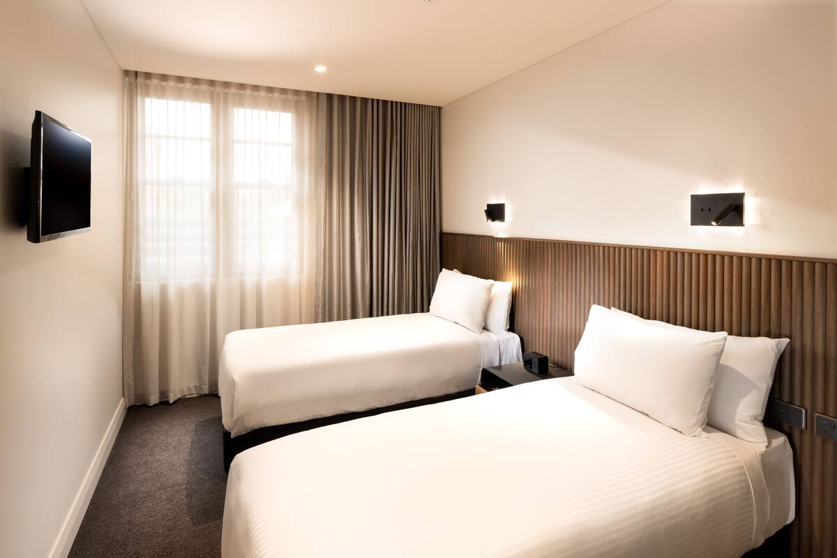 Quarto de hotel com duas camas, televisão de tela plana e janela com cortinas.
