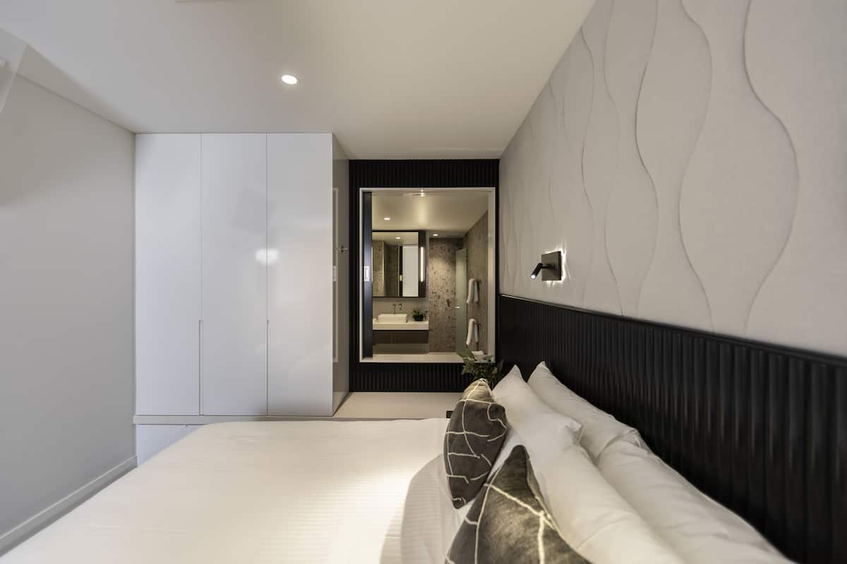 Um quarto moderno com uma cama grande, um guarda-roupa, um espelho e uma parede com padrão ondulado.