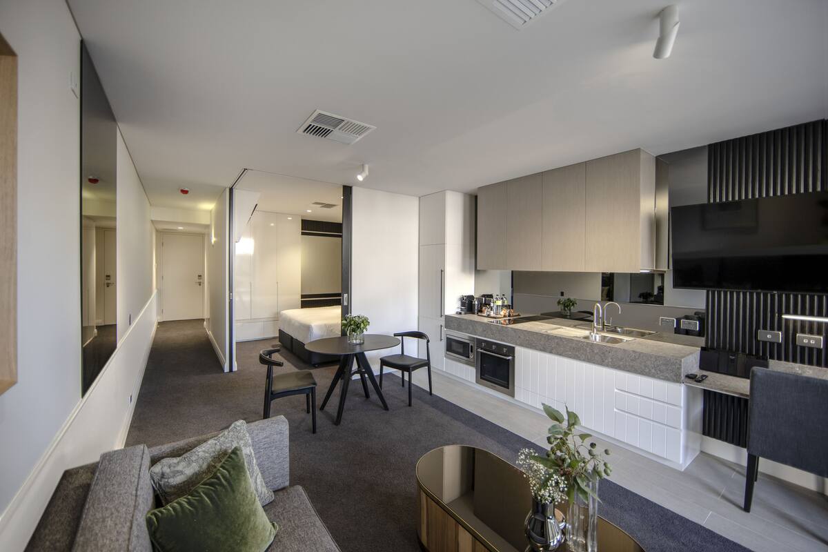 Cozinha moderna com ilha central, área de refeições com mesa e cadeiras, e sala de estar com sofá e mesa de centro.