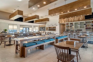 Um restaurante amplo com pé-direito alto, vigas de madeira e luminárias modernas.