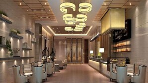Um lobby moderno de hotel com uma recepção central, área de estar e um lustre decorativo.