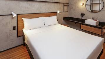 Quarto de hotel moderno com uma cama grande, abajures, um espelho redondo, mesa de cabeceira de madeira e uma estante embutida com uma pia.