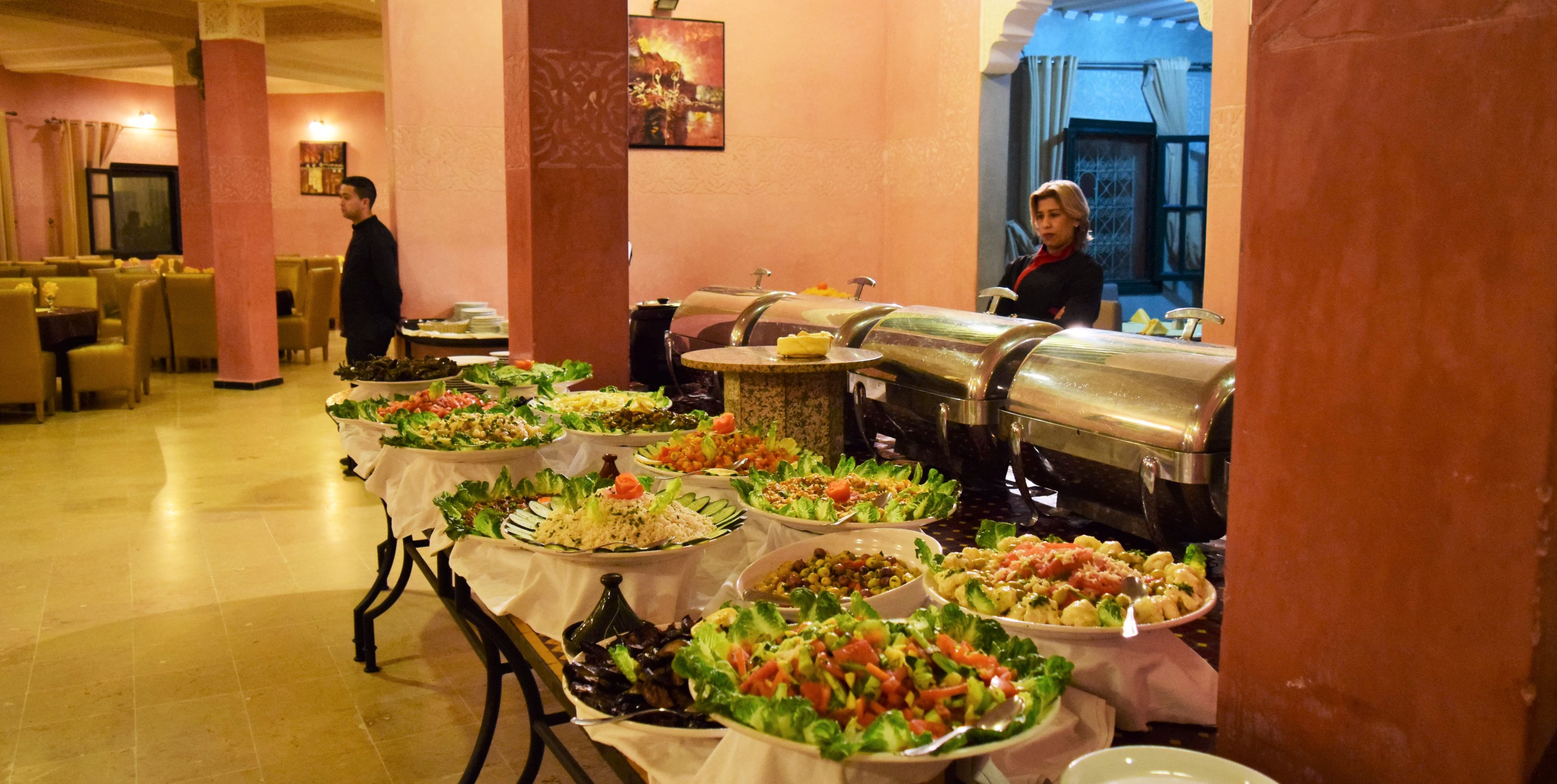 Disposição de buffet com diversos pratos, uma linha de buffet e uma pessoa servindo.