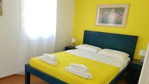 Uma cama com um edredom amarelo e duas almofadas brancas, uma mesa de cabeceira com abajur e um quadro na parede.