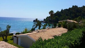 Um imóvel costeiro com telhado de cerâmica, vista para o mar e vegetação exuberante.