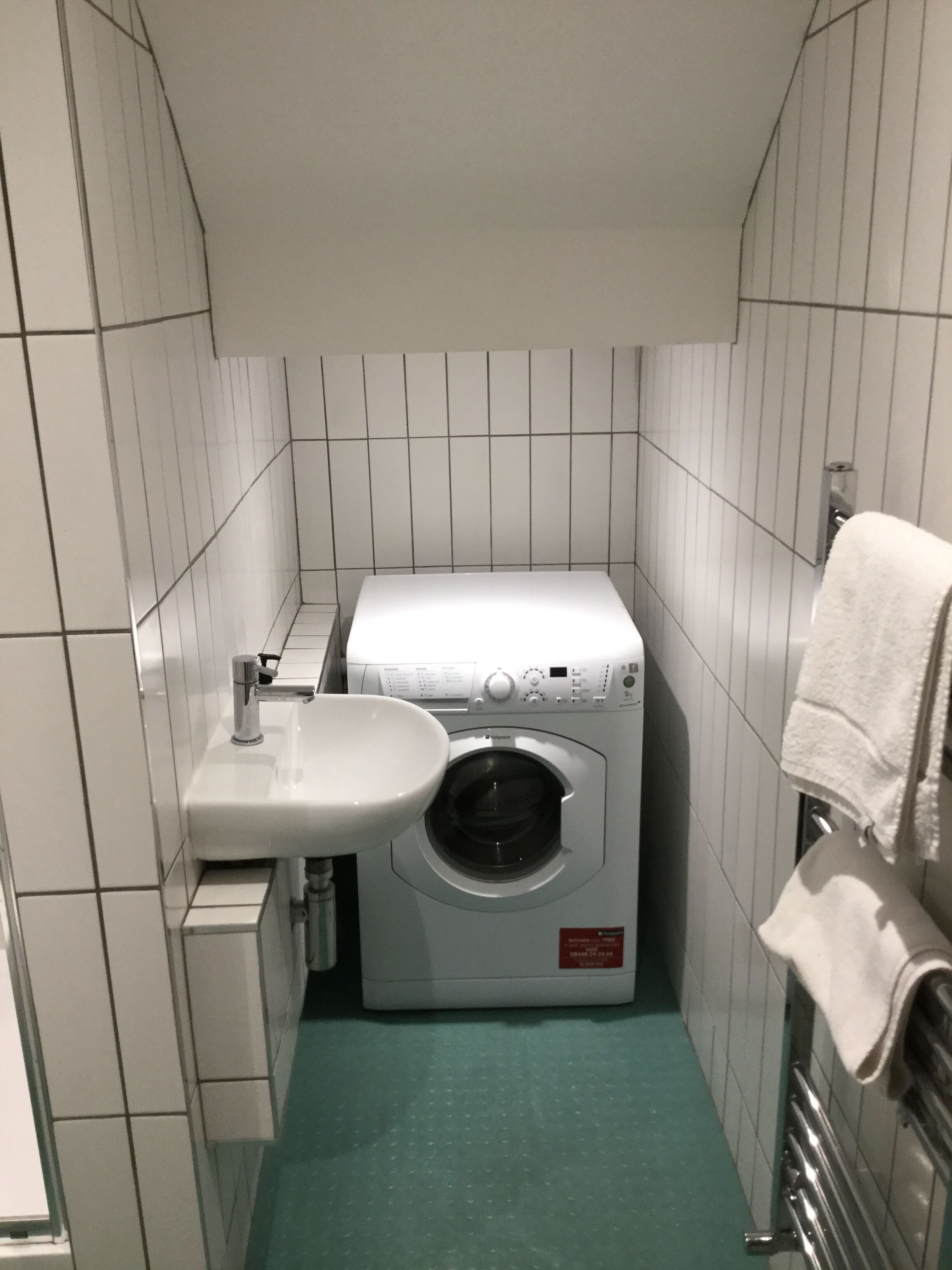 Uma lavanderia compacta com máquina de lavar, pia e porta-toalhas.