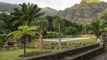 Uma piscina rodeada por palmeiras e uma parede de pedra, com montanhas ao fundo.
