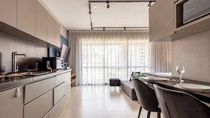 Cozinha moderna com área de jantar, apresentando televisão de tela plana, eletrodomésticos embutidos e uma grande janela com cortinas leves.