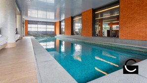Piscina interior com água azul cristalina, rodeada por um design moderno com elementos de tijolo e vidro.