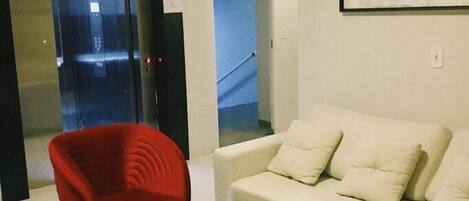 Uma sala de estar moderna com uma poltrona vermelha, um sofá branco e uma mesa de centro de vidro.