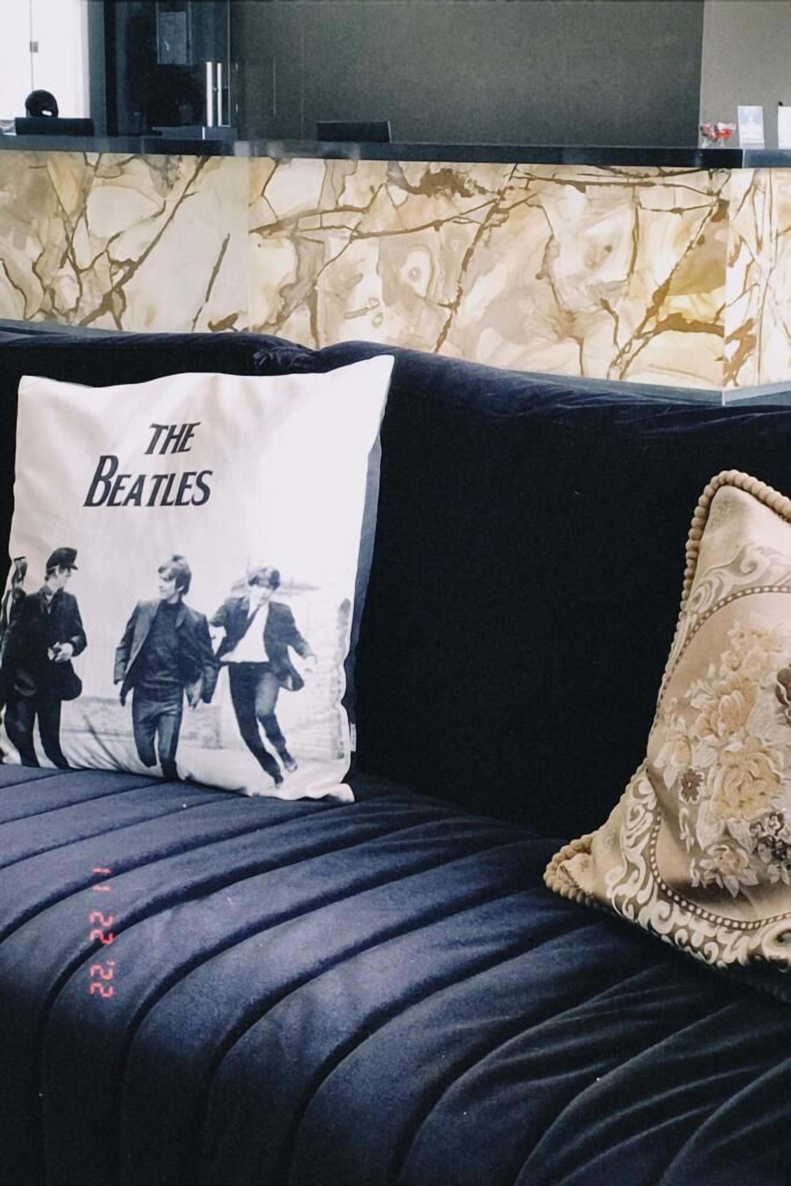 Um sofá escuro com uma almofada com The Beatles e outra almofada decorada com estampas florais.