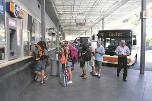 Uma rodoviária com um relógio digital mostrando 10:16, um ônibus com a inscrição 'Cavist' e pessoas aguardando.