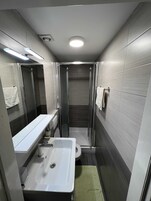Um banheiro moderno com pia branca, espelho, vaso sanitário e box.