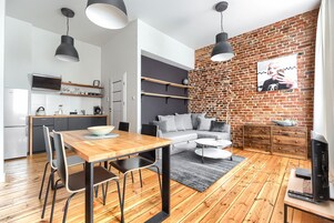 Cozinha moderna com área de refeições, sala de estar com sofá e mesa de centro, e parede de tijolos com uma imagem.