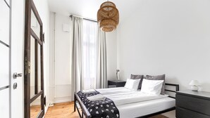 Um quarto com cama, mesas de cabeceira, cômoda, luminária pendente e uma porta.