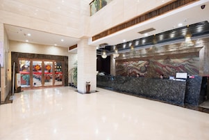 Um hall amplo com balcão de recepção, um grande mural e entrada por porta de vidro.