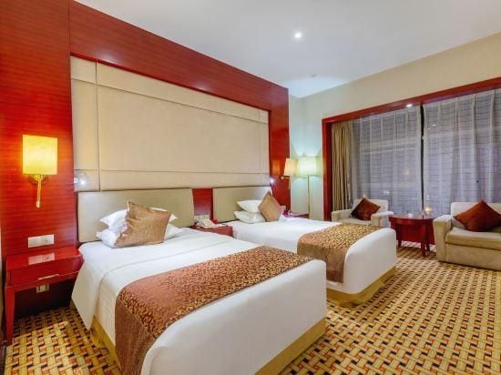 Quarto de hotel com duas camas, um sofá e uma grande janela com cortinas.