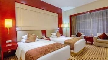 Quarto de hotel com duas camas, um sofá e uma grande janela com cortinas.