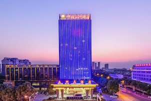 Um hotel imponente com linhas verticais de luzes, uma entrada ampla e paisagem urbana ao fundo.