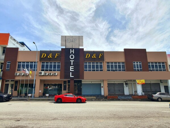 Um hotel D&F com fachada moderna, grandes janelas e um carro esportivo vermelho estacionado na frente.