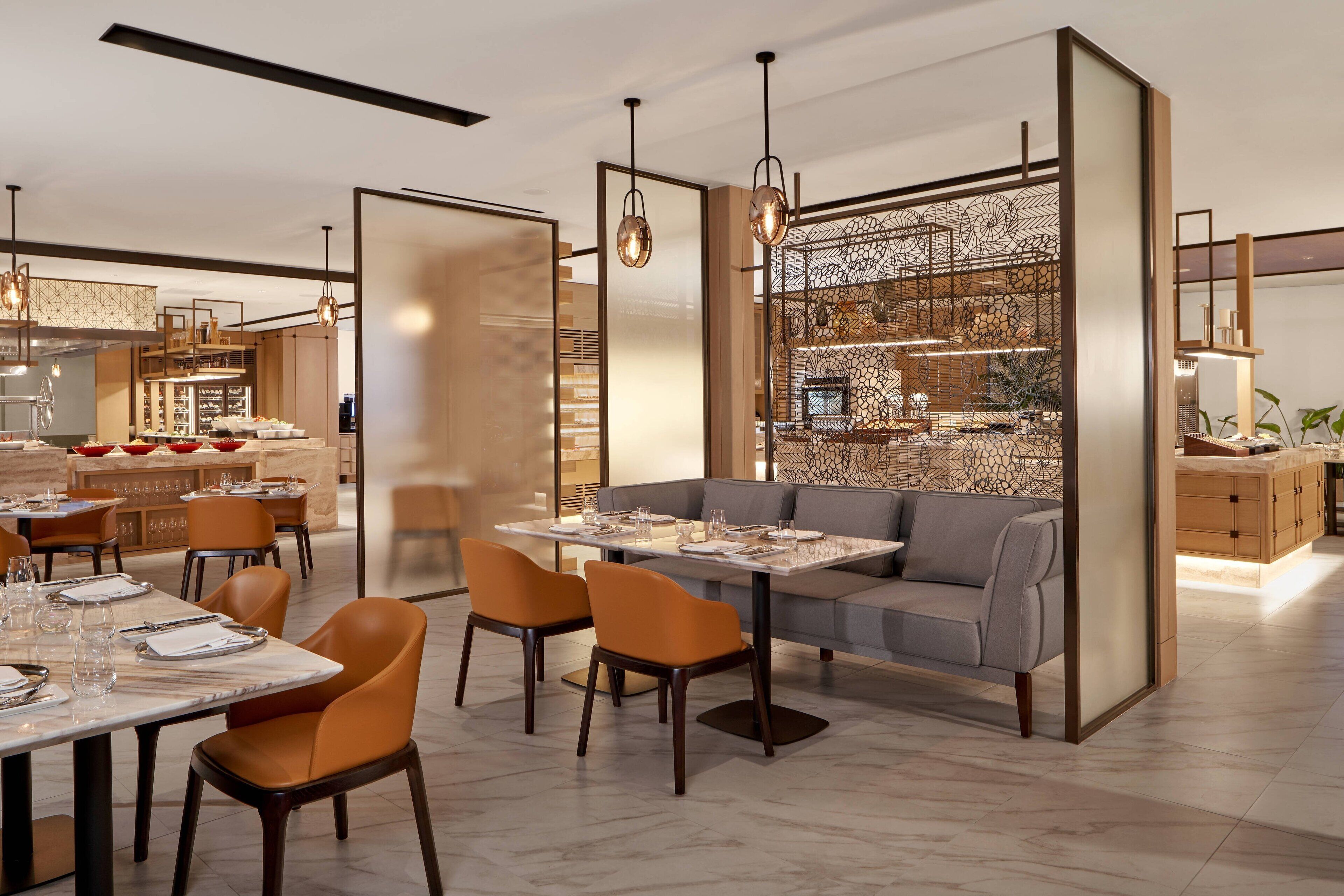 Uma sala de jantar moderna com um sofá cinzento, cadeiras laranja e uma mesa de mármore posta para quatro pessoas.