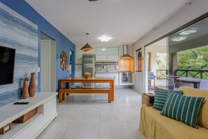 Uma sala de estar moderna com uma televisão de tela plana, uma mesa de jantar de madeira e um sofá com almofadas listradas.