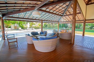 Uma área de estar coberta ao ar livre, com móveis de vime e um deck de madeira.