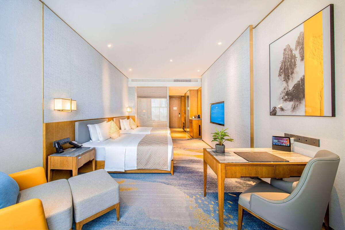Quarto de hotel com cama, mesa de cabeceira, escrivaninha, cadeira e uma grande pintura na parede.