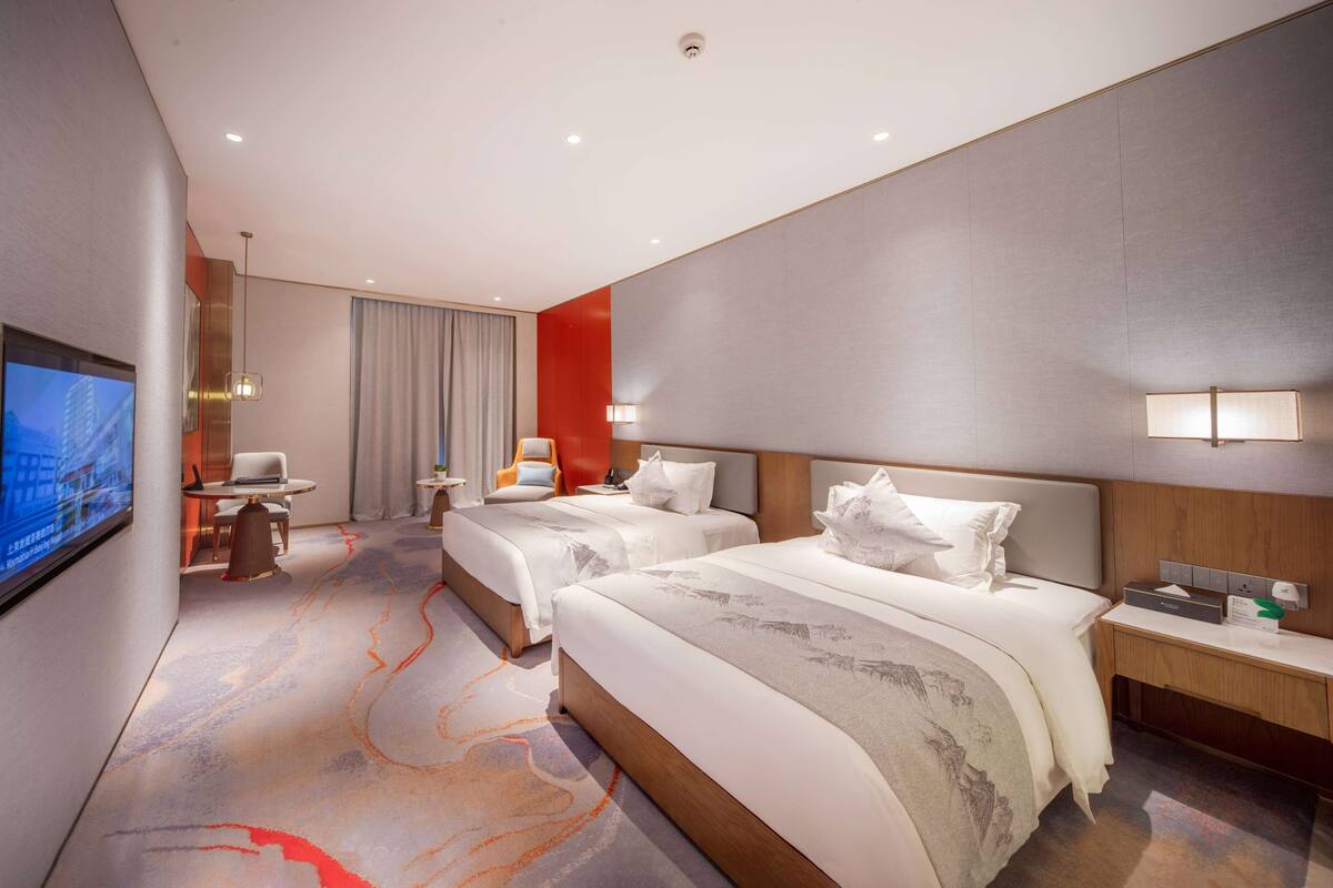 Quarto de hotel com duas camas, uma televisão, uma escrivaninha e uma cadeira.